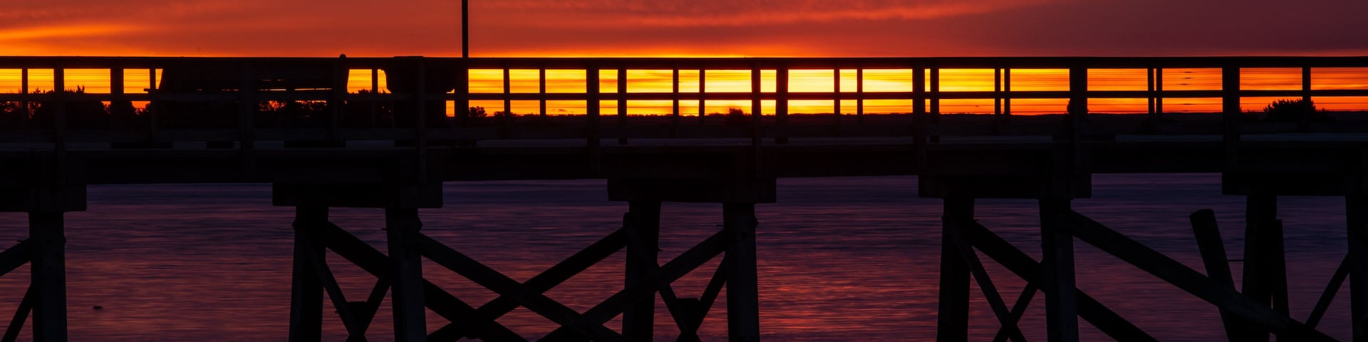 Um pôr do sol sobre a água, com um cais e um poste de luz.