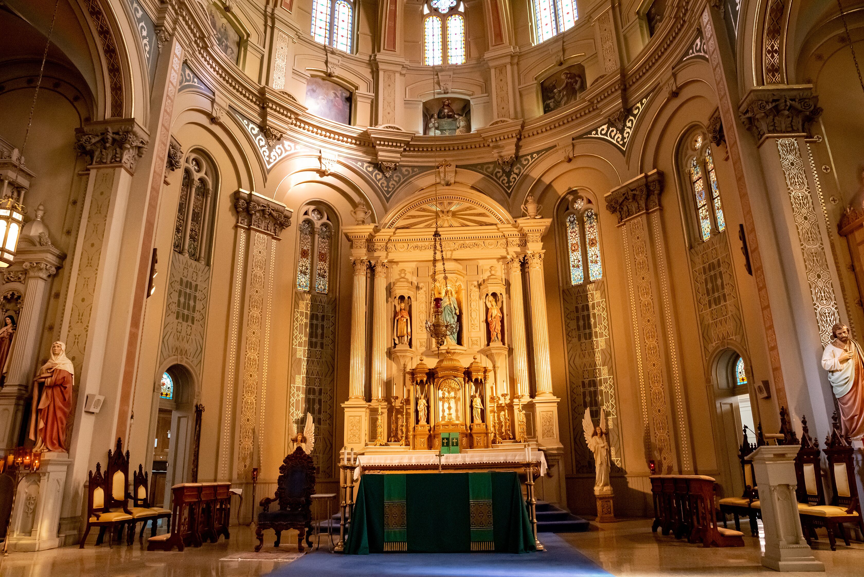 Interior de igreja ornamentado com altar central, estátuas e vitrais.