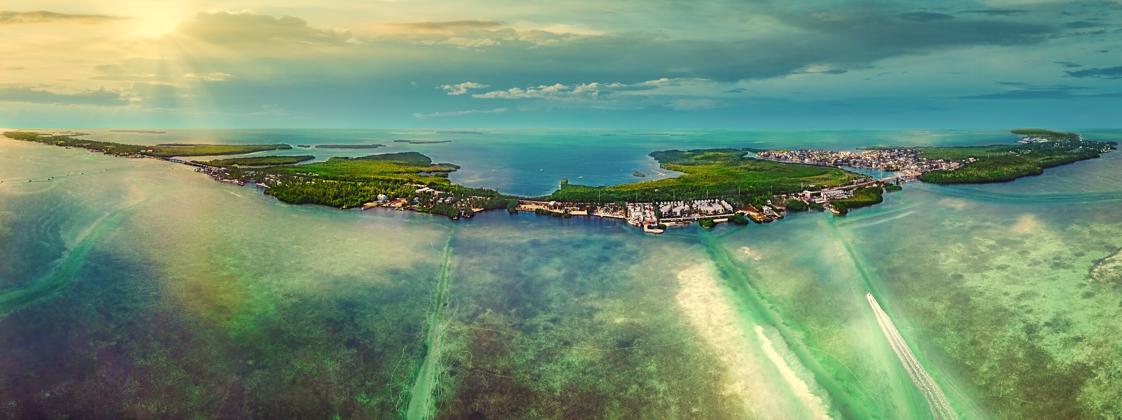 Vista aérea de uma vila costeira com um porto de recreio, rodeada por águas azuis cristalinas e ilhas verdes.