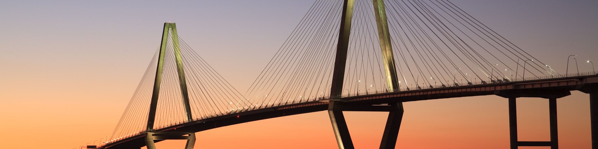 Uma ponte com design de cabos característico, atravessando um corpo de água ao pôr do sol.