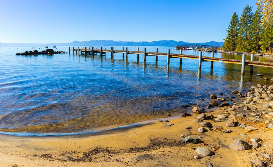 Um lago límpido com um cais de madeira que se estende pela água, rodeado por rochas e árvores.