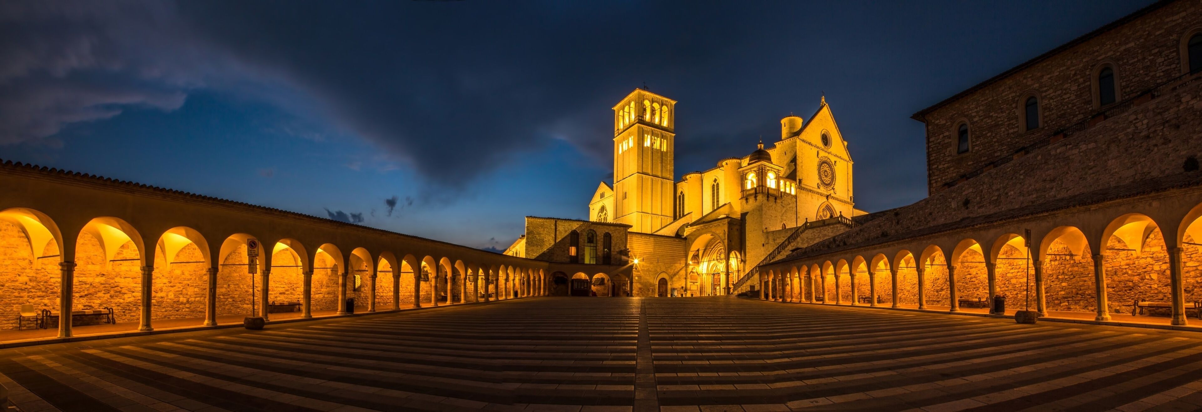 Uma catedral com uma alta torre sineira e um pátio com arcos.