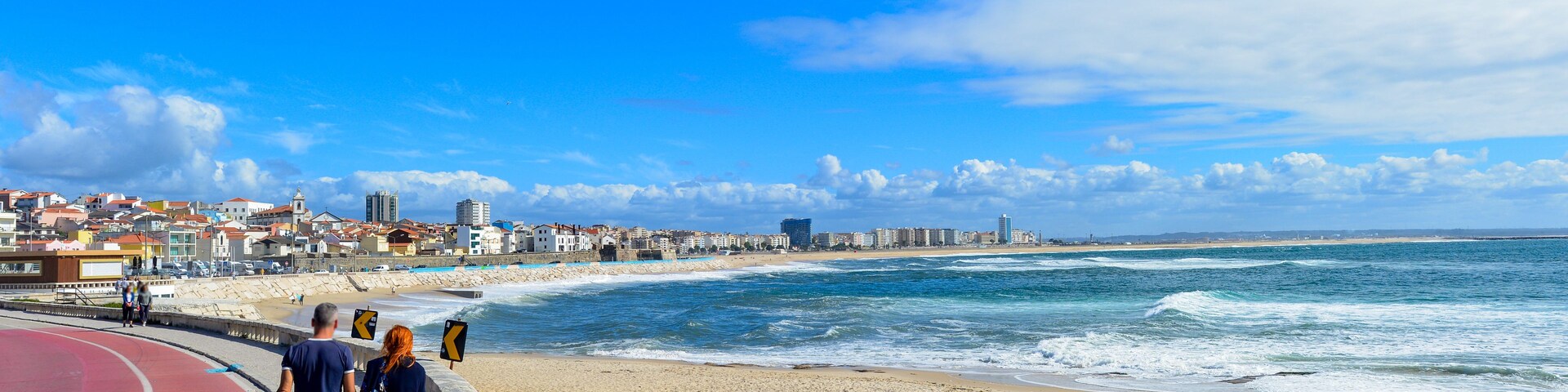Paisagem costeira urbana com praia, pista de corrida e céu azul límpido.