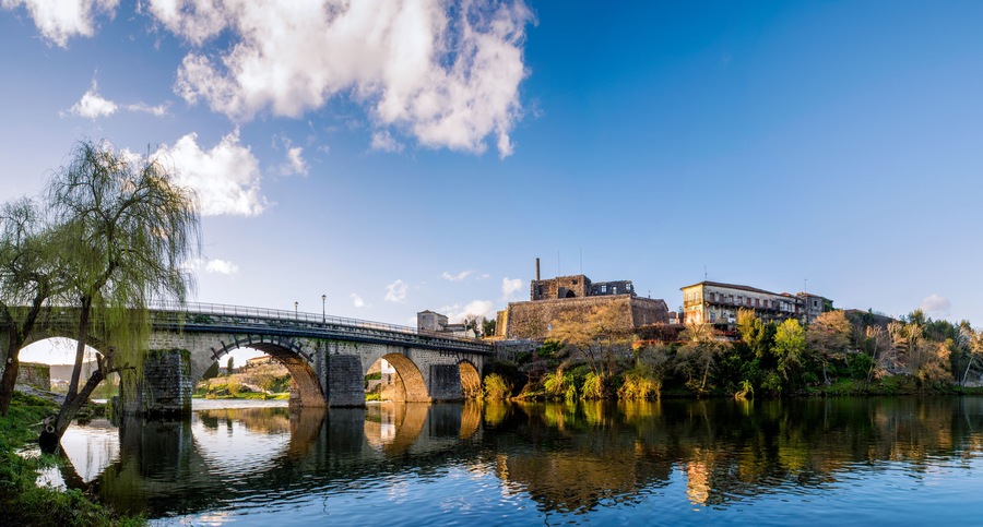 Uma ponte de pedra sobre um rio, um castelo e um céu claro.