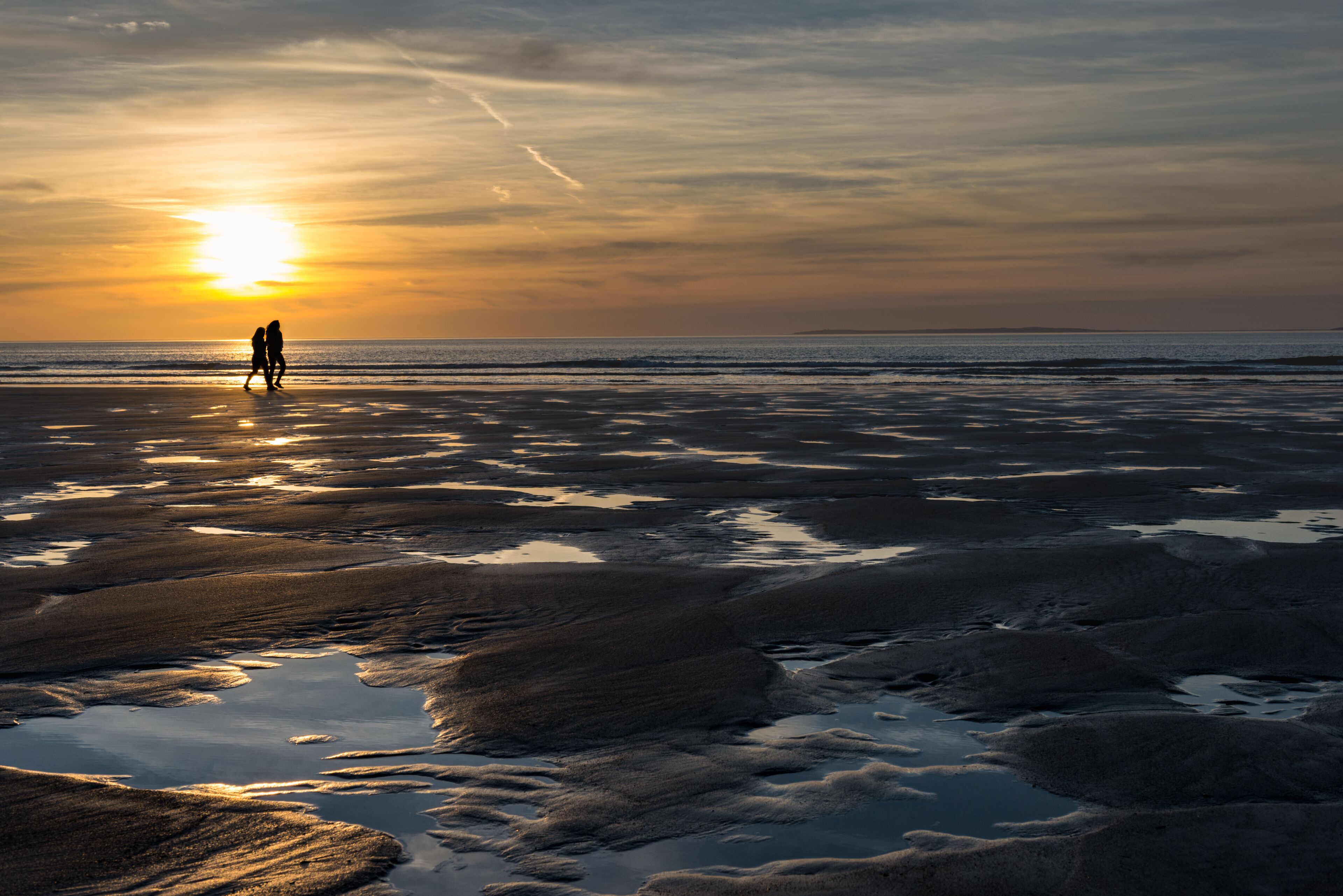 Pôr do sol sobre uma praia com pessoas caminhando, e céu limpo.