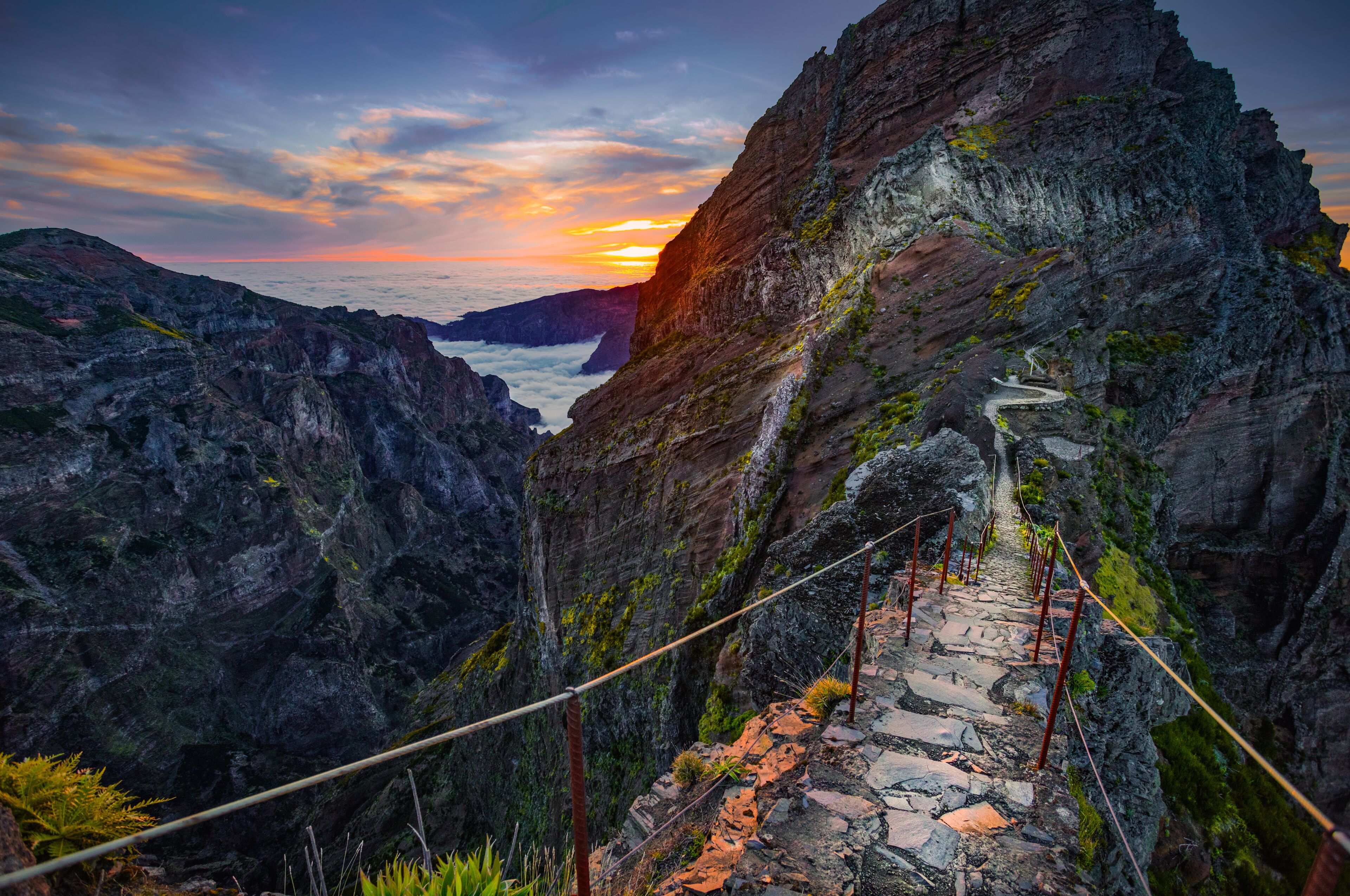 Trilha rochosa na montanha com um pôr do sol ao fundo.