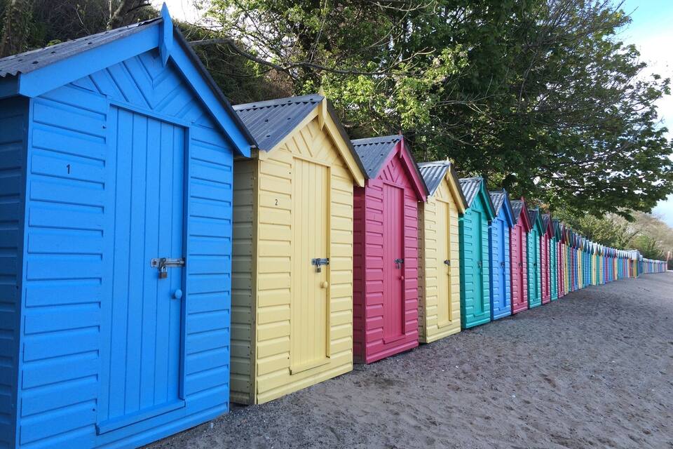 Uma fileira de cabanas de praia coloridas, com portas numeradas.