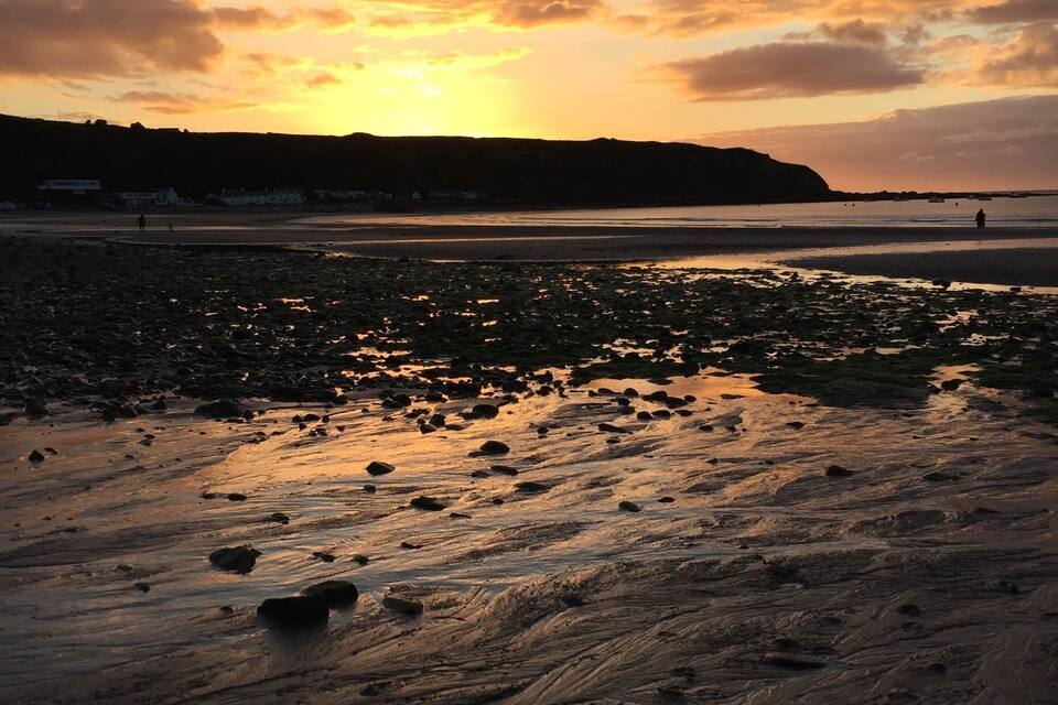 Uma praia ao pôr do sol com costa rochosa e colinas ao longe.