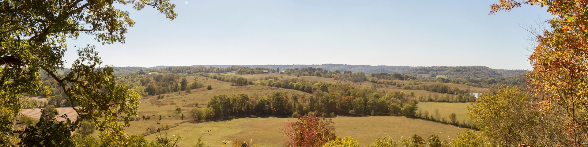 Paisagem acidentada com céu limpo, cercada por árvores e campos.