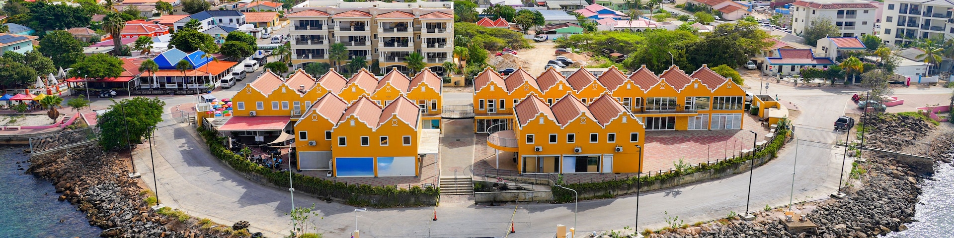 Uma vila costeira com edifícios coloridos, mar azul cristalino e um litoral rochoso.