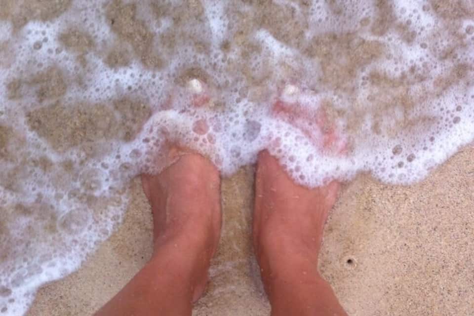 Pés em areia molhada com água espumosa.