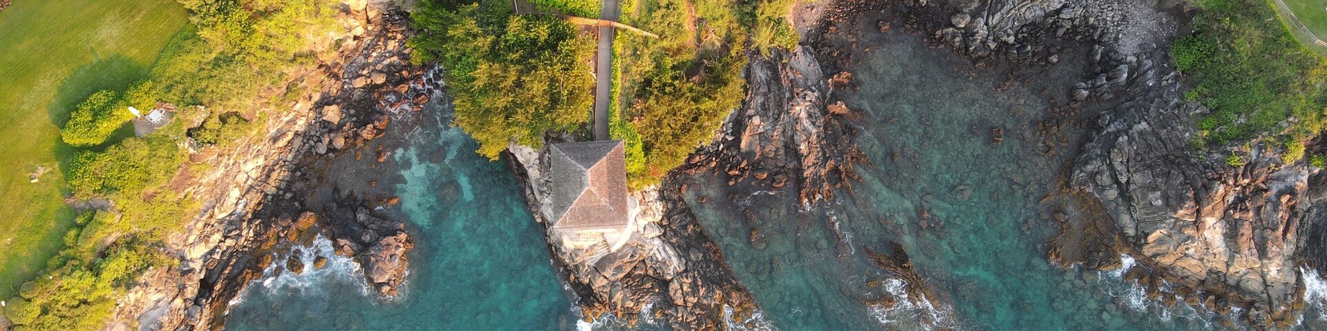 Paisagem costeira com águas turquesa cristalinas, falésias rochosas e uma pequena casa à beira do penhasco.