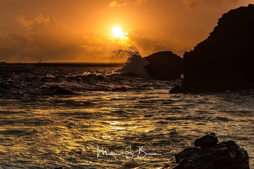 Um pôr do sol sobre o oceano com ondas quebrando nas rochas.