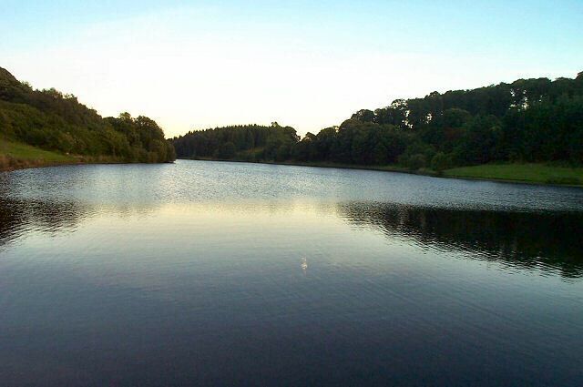 Um lago calmo rodeado por colinas arborizadas.