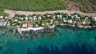 Vista aérea de uma área residencial costeira com casas, praia e águas turquesa cristalinas.