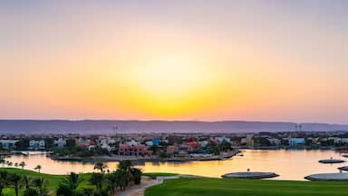 Um pôr do sol sobre um campo de golfe com um lago e edifícios ao fundo.