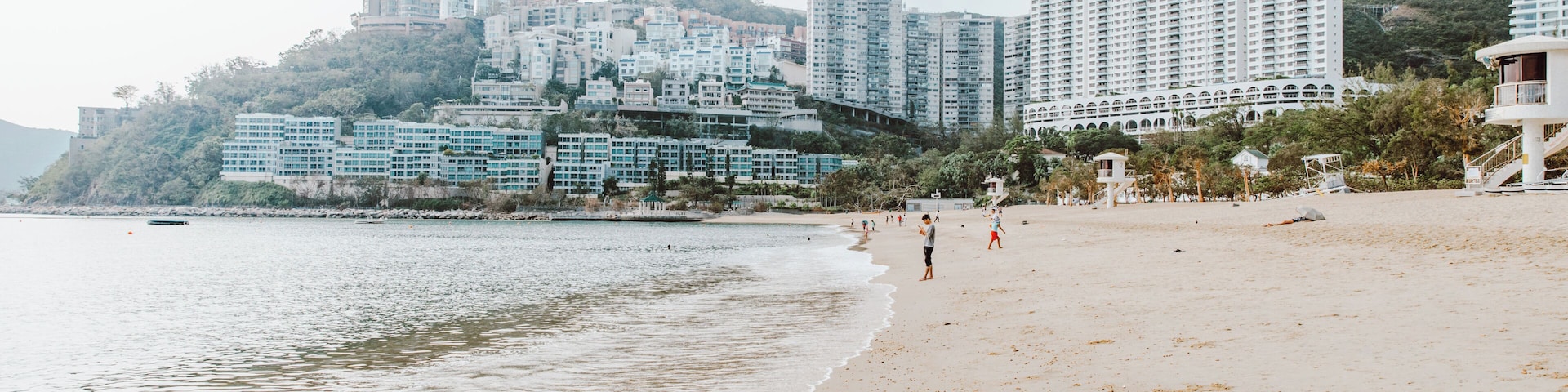Uma praia com pessoas, areal arenoso e edifícios altos ao fundo.