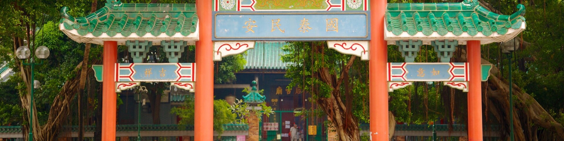 Um portão tradicional chinês com decorações elaboradas em verde e branco, rodeado por vegetação exuberante e árvores.