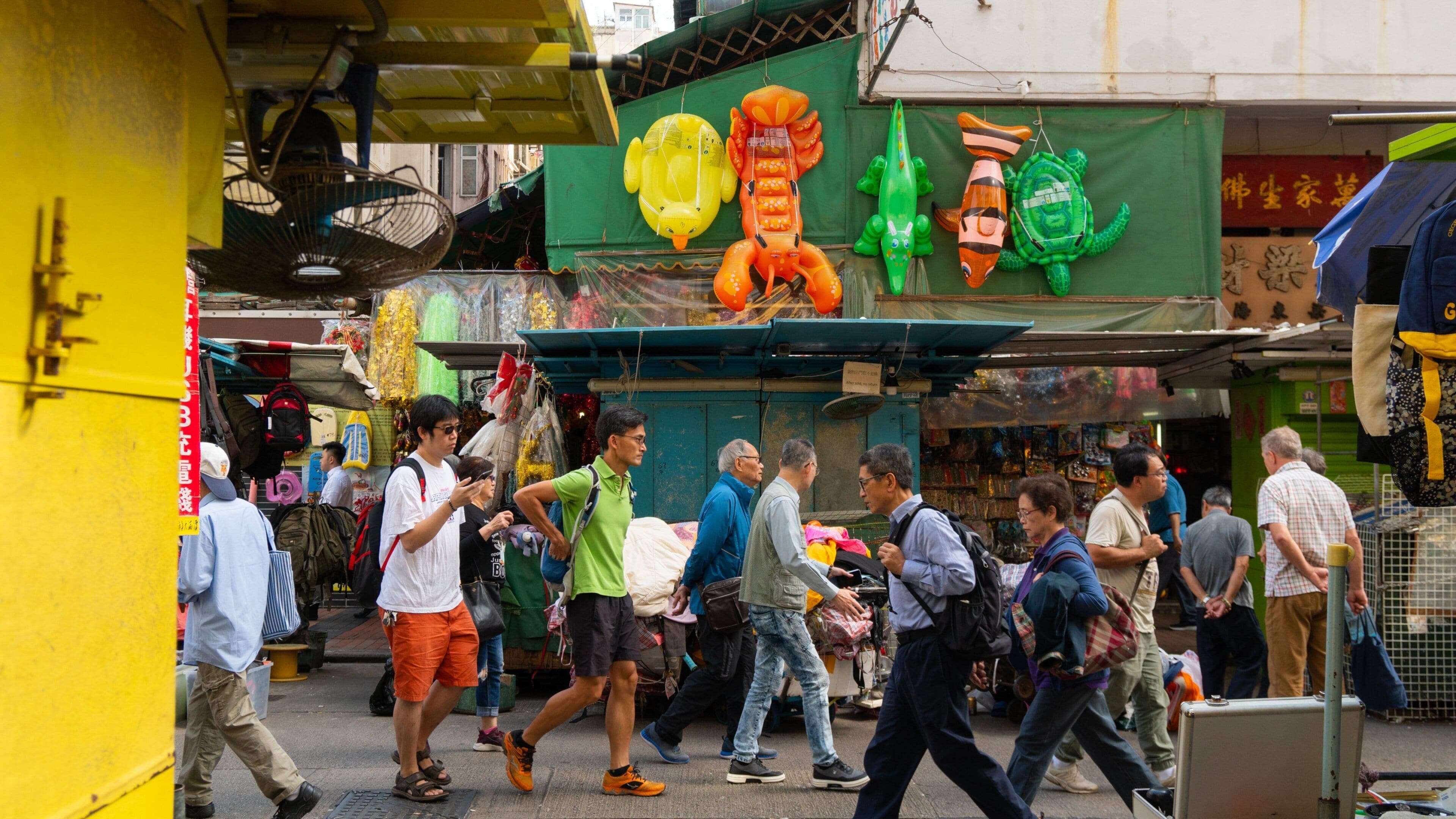 Mercado de rua movimentado com decorações coloridas, incluindo grandes criaturas marinhas infláveis e um toldo verde.