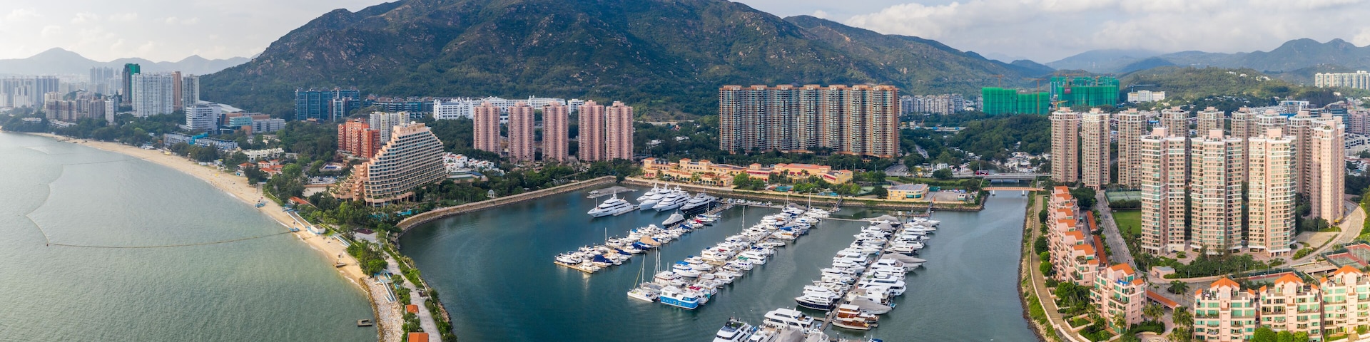 Marina com vários barcos atracados, cercada por edifícios residenciais altos e um cenário montanhoso.
