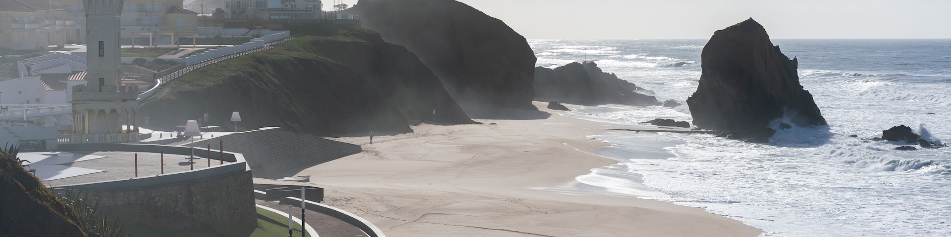 Uma vila costeira com um farol, uma praia e afloramentos rochosos.