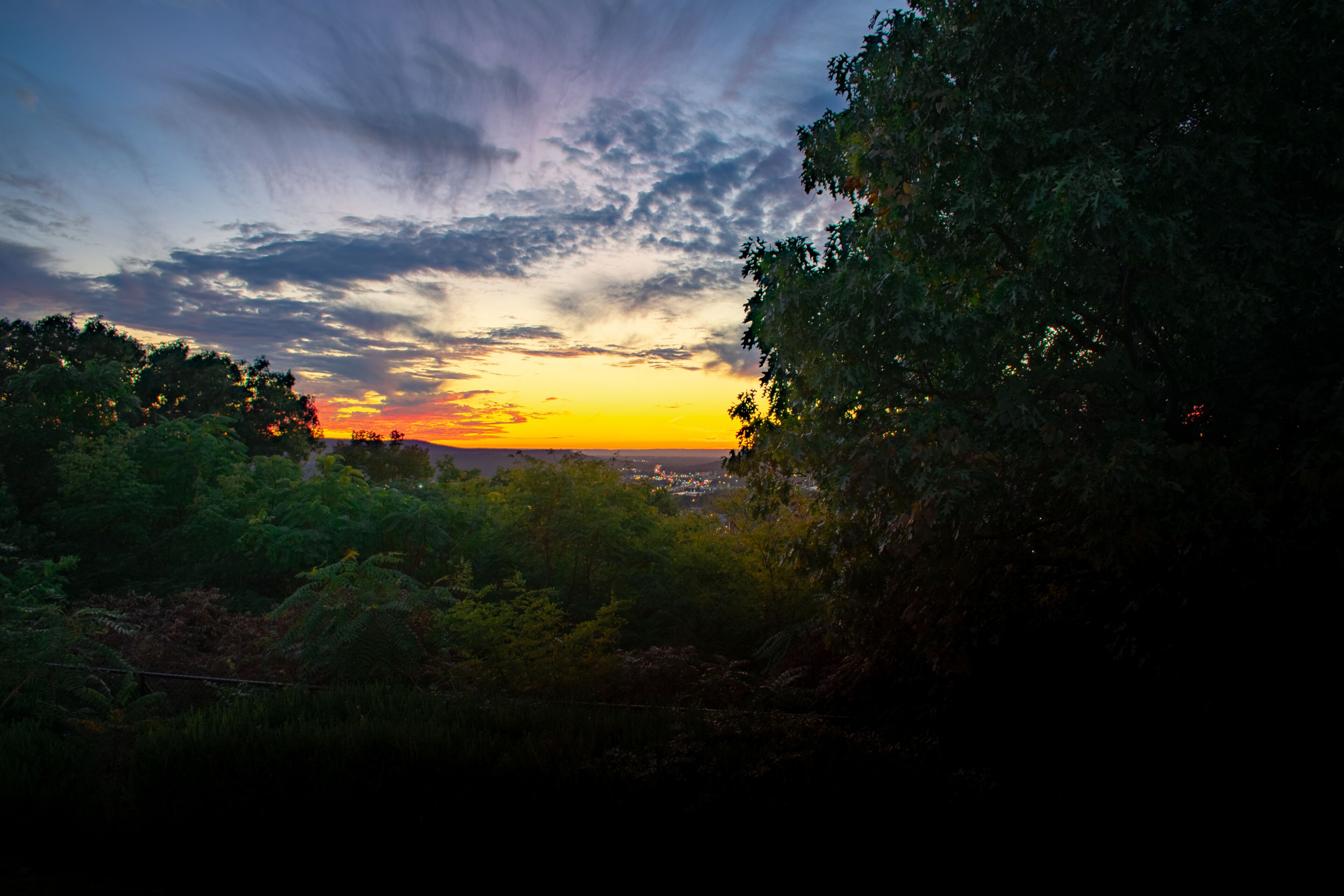 Um pôr do sol sobre uma paisagem arborizada com vista para uma cidade distante.