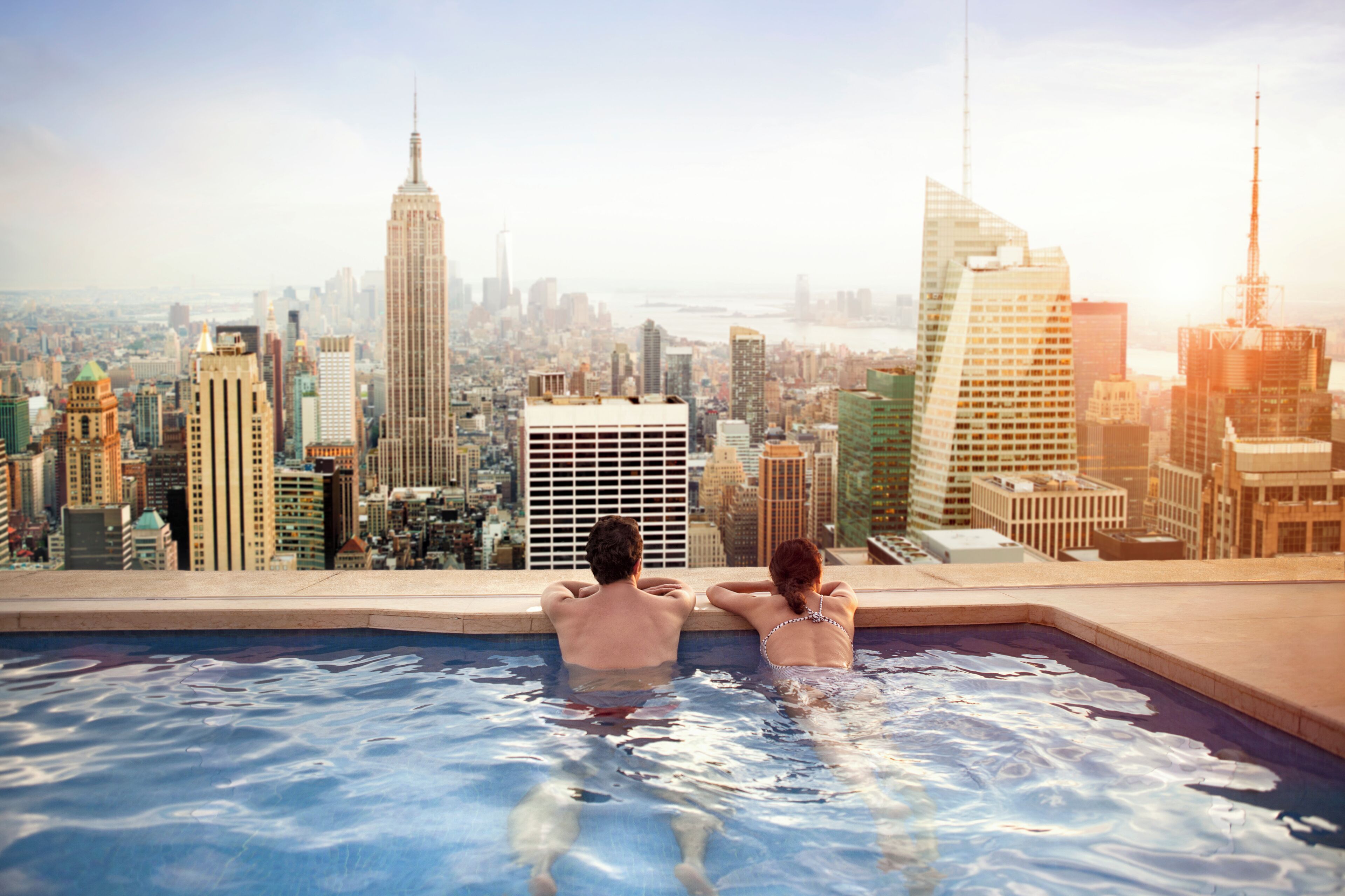 Um casal relaxando em uma piscina com vista para um horizonte urbano e arranha-céus imponentes.