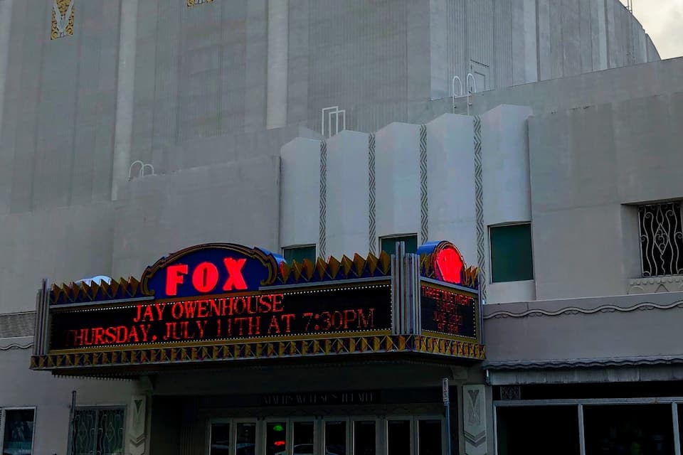 Um edifício grande com um letreiro 'FOX' e um letreiro anunciando 'Jay Owenhouse' às 19h30 de 19 de julho.