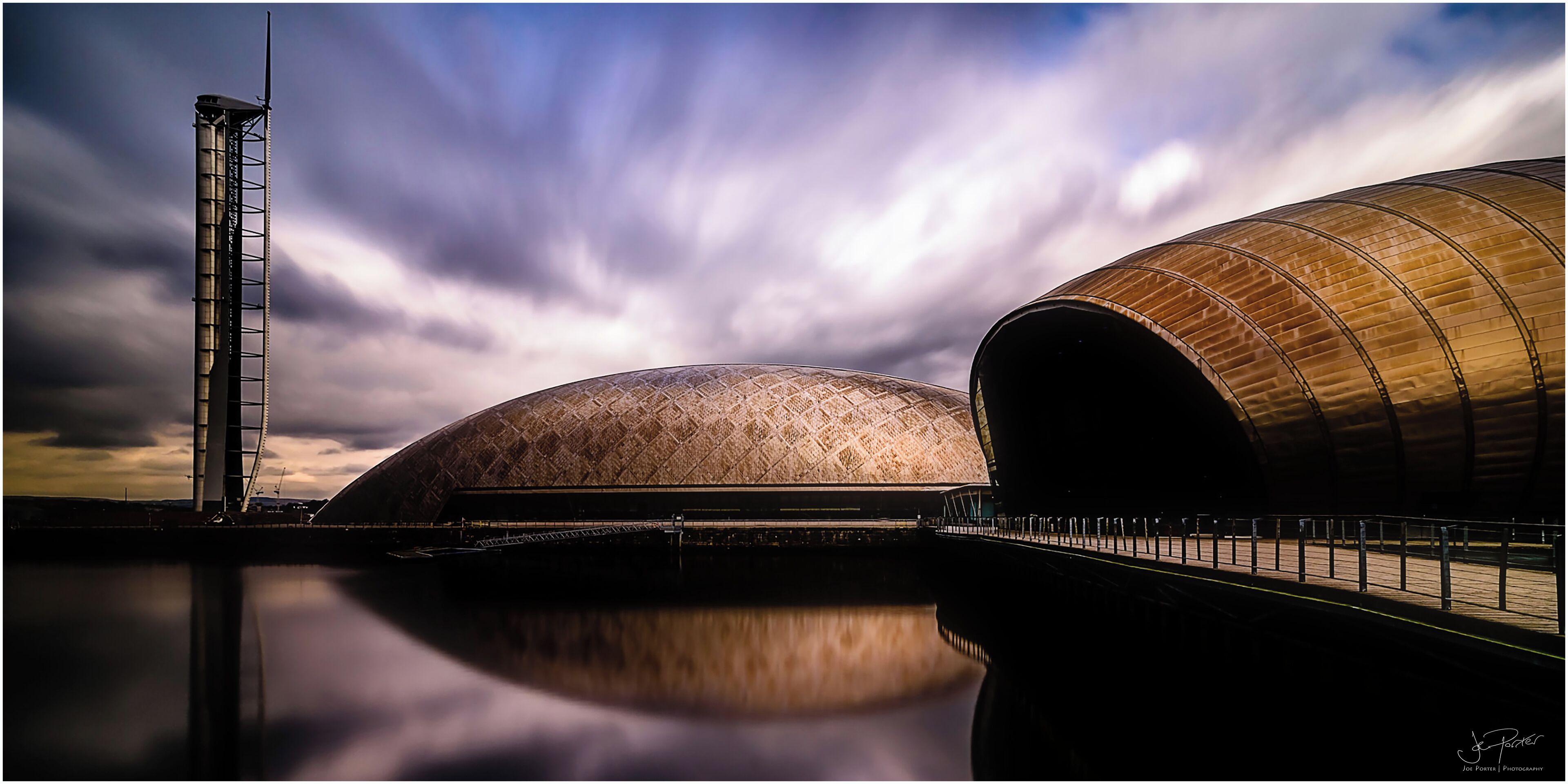 Um estádio grande e moderno com um design de teto curvo e único, refletindo na água abaixo.