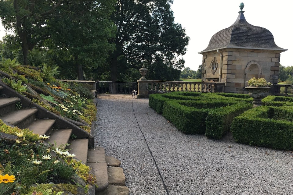 Um jardim com um edifício de pedra, um caminho de cascalho e sebes bem aparadas.
