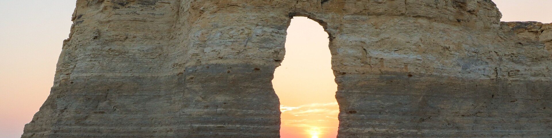 Grande formação rochosa com um arco ao pôr do sol.