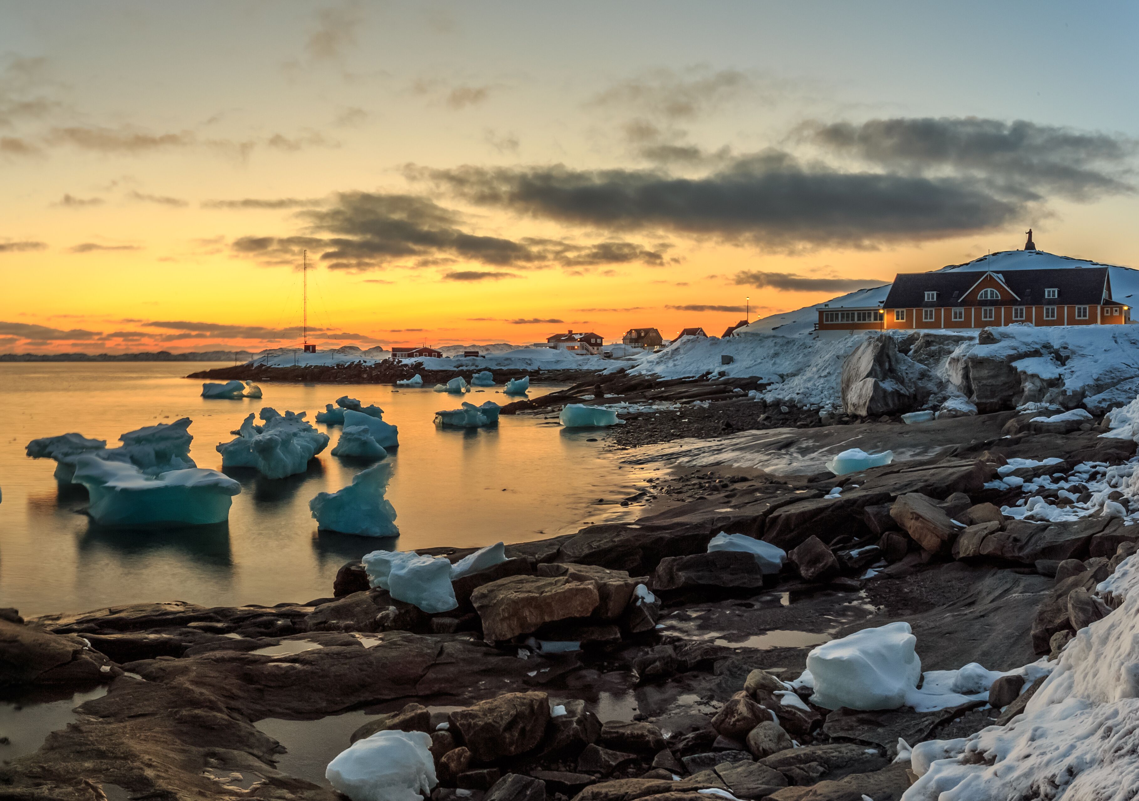 Paisagem costeira com icebergs, uma casa e um pôr do sol.