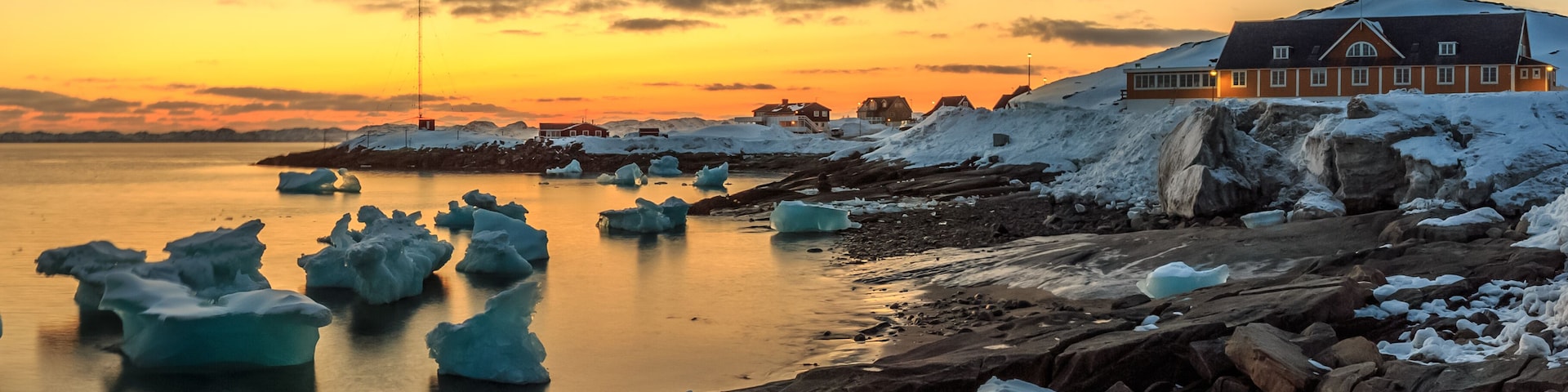 Paisagem costeira com icebergs, uma casa e um pôr do sol.