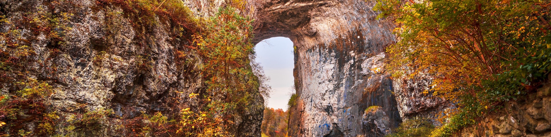 Um arco de pedra cercado por folhagem outonal, bancos e um muro de pedra.