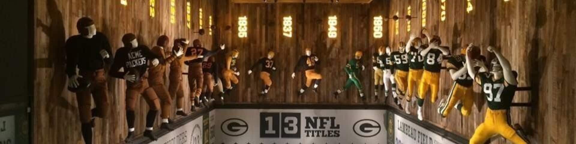 Museu esportivo com estátuas de jogadores de futebol e uma placa indicando 13 títulos da NFL.