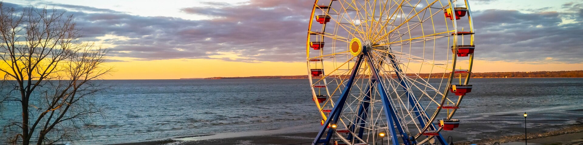 Uma grande roda gigante à beira-mar com o pôr do sol ao fundo.
