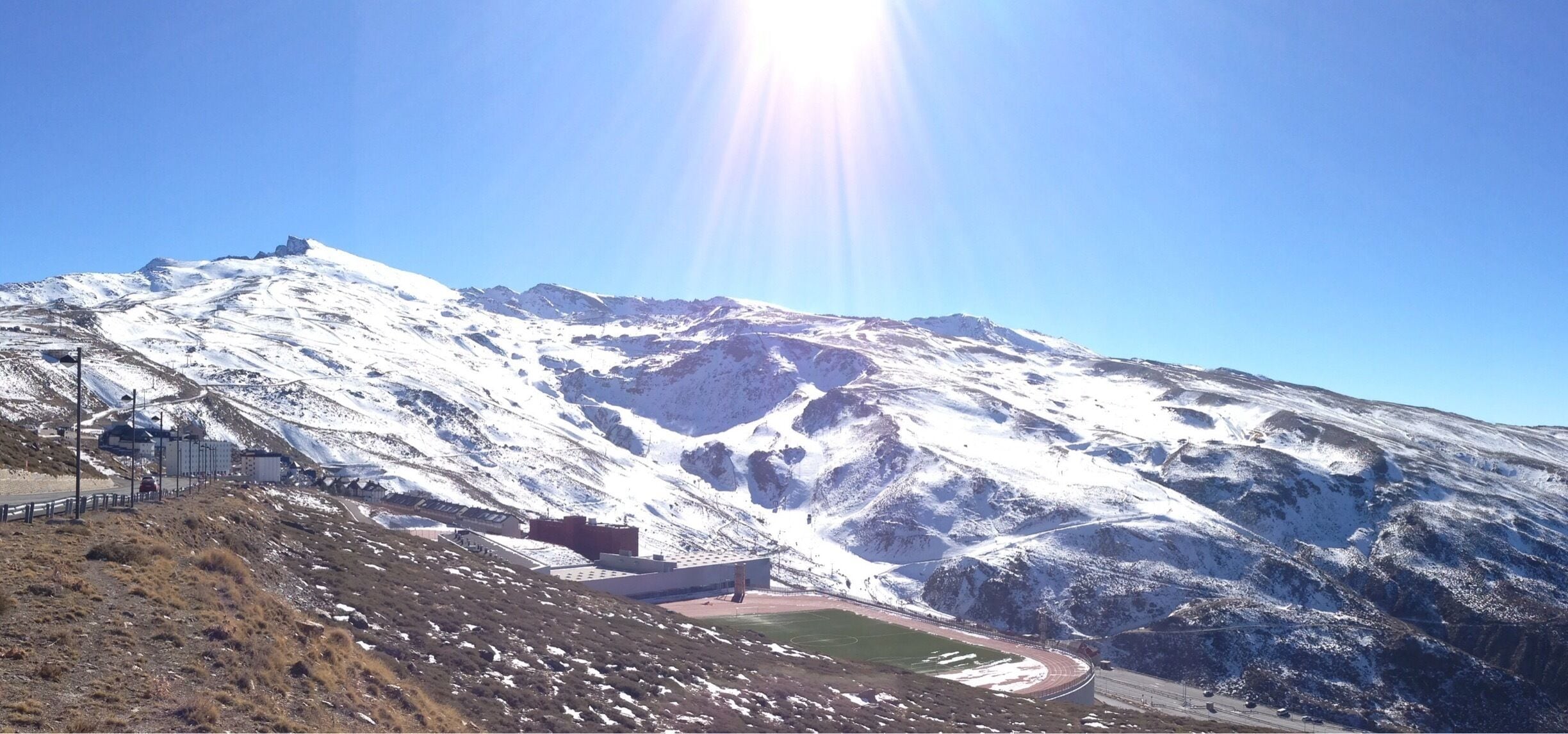 Montanha coberta de neve com céu claro e sol brilhando.