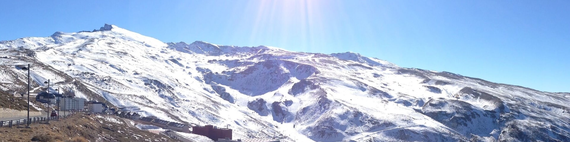 Montanha coberta de neve com céu claro e sol brilhando.