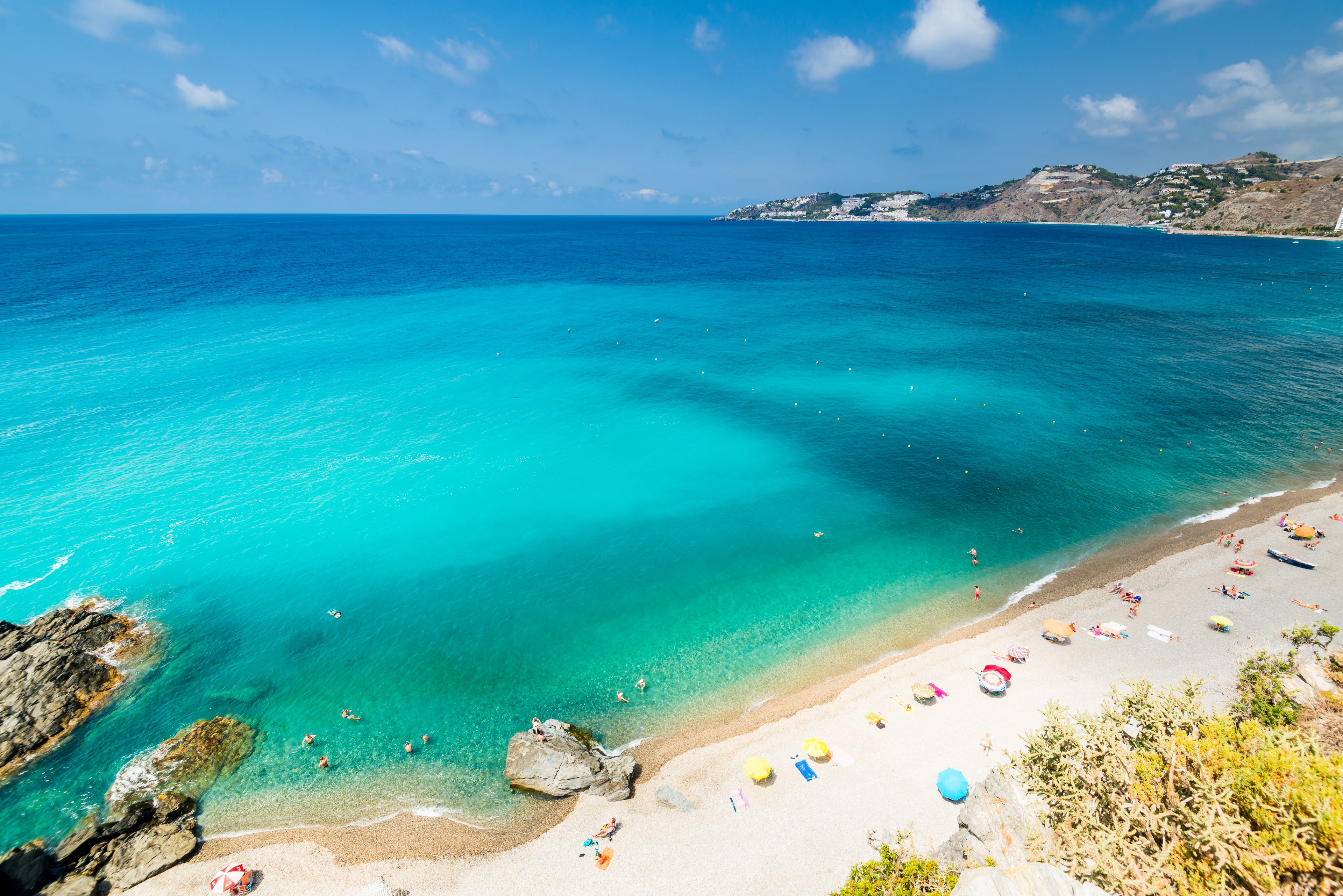 Mar turquesa com águas cristalinas, uma praia de areia e um litoral rochoso.