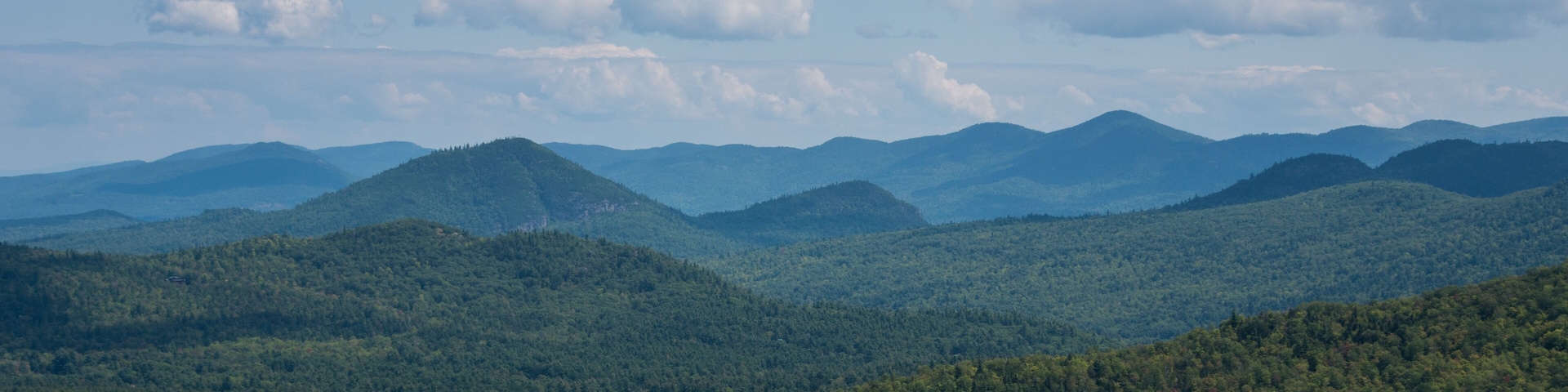 Paisagem montanhosa com florestas densas e colinas ondulantes sob um céu parcialmente nublado.