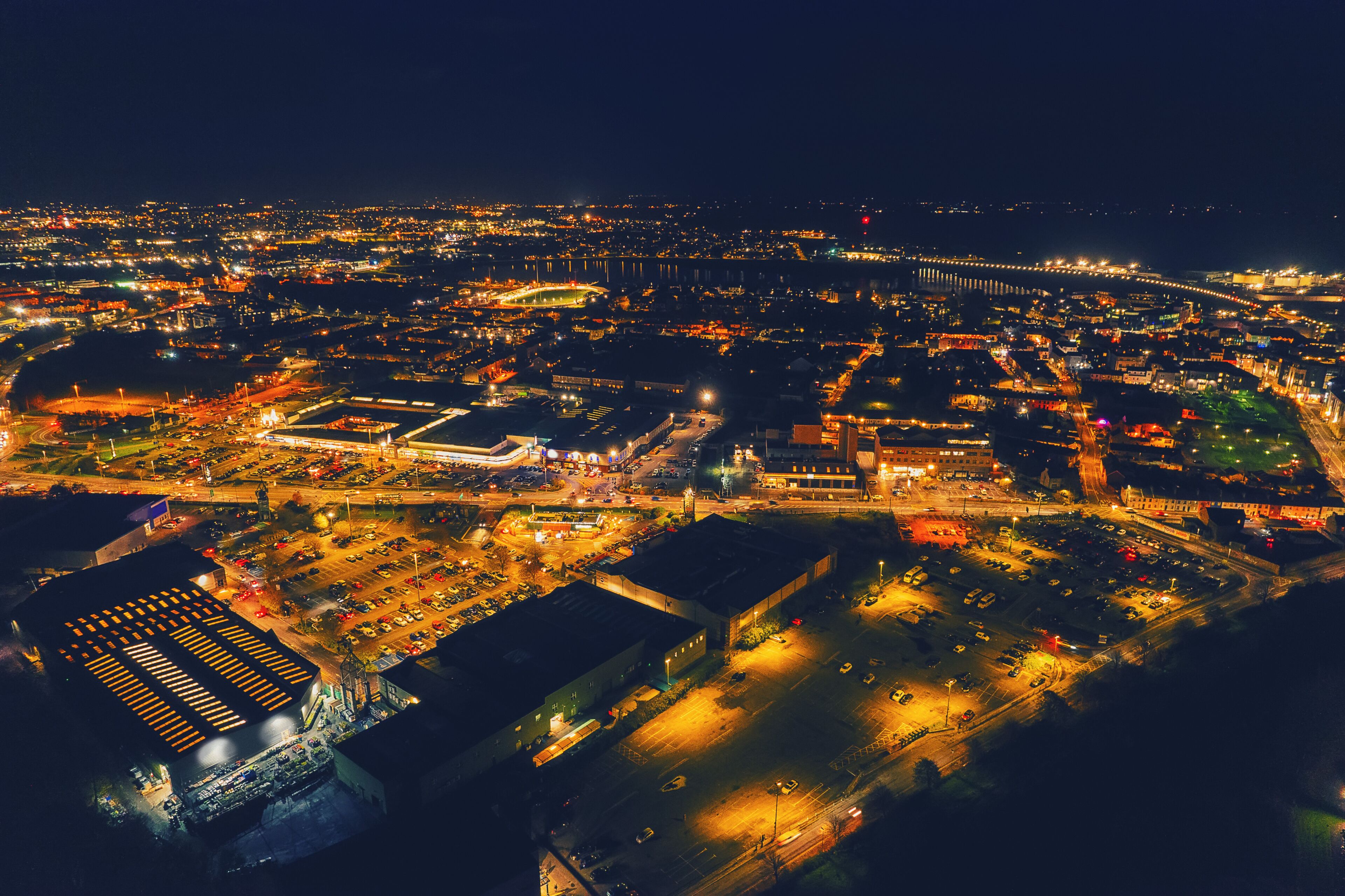 Vista aérea de uma cidade à noite, com edifícios, ruas e um estádio iluminados.