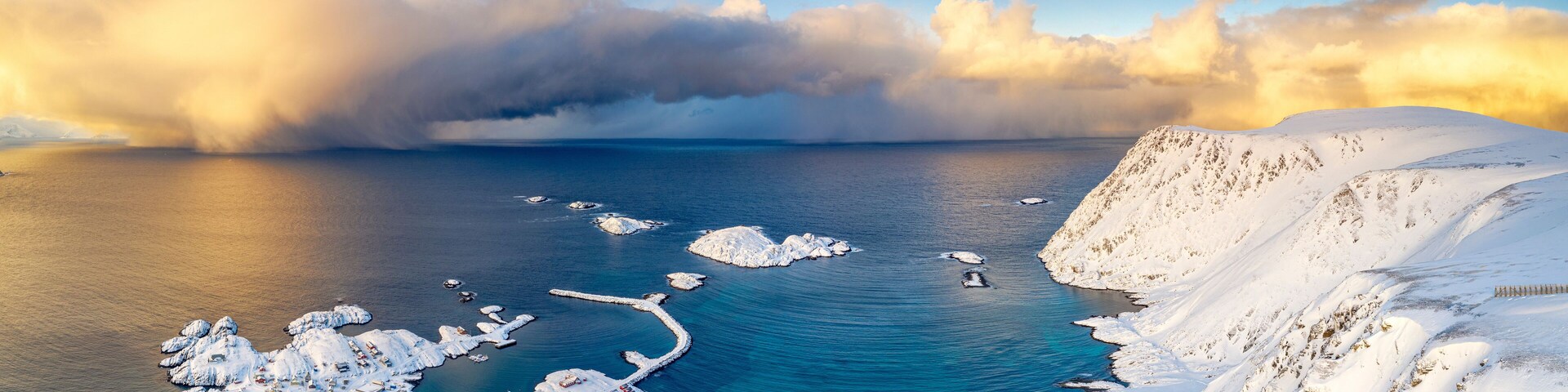 Paisagem costeira nevada com icebergs, mar azul cristalino e montanha coberta de neve.