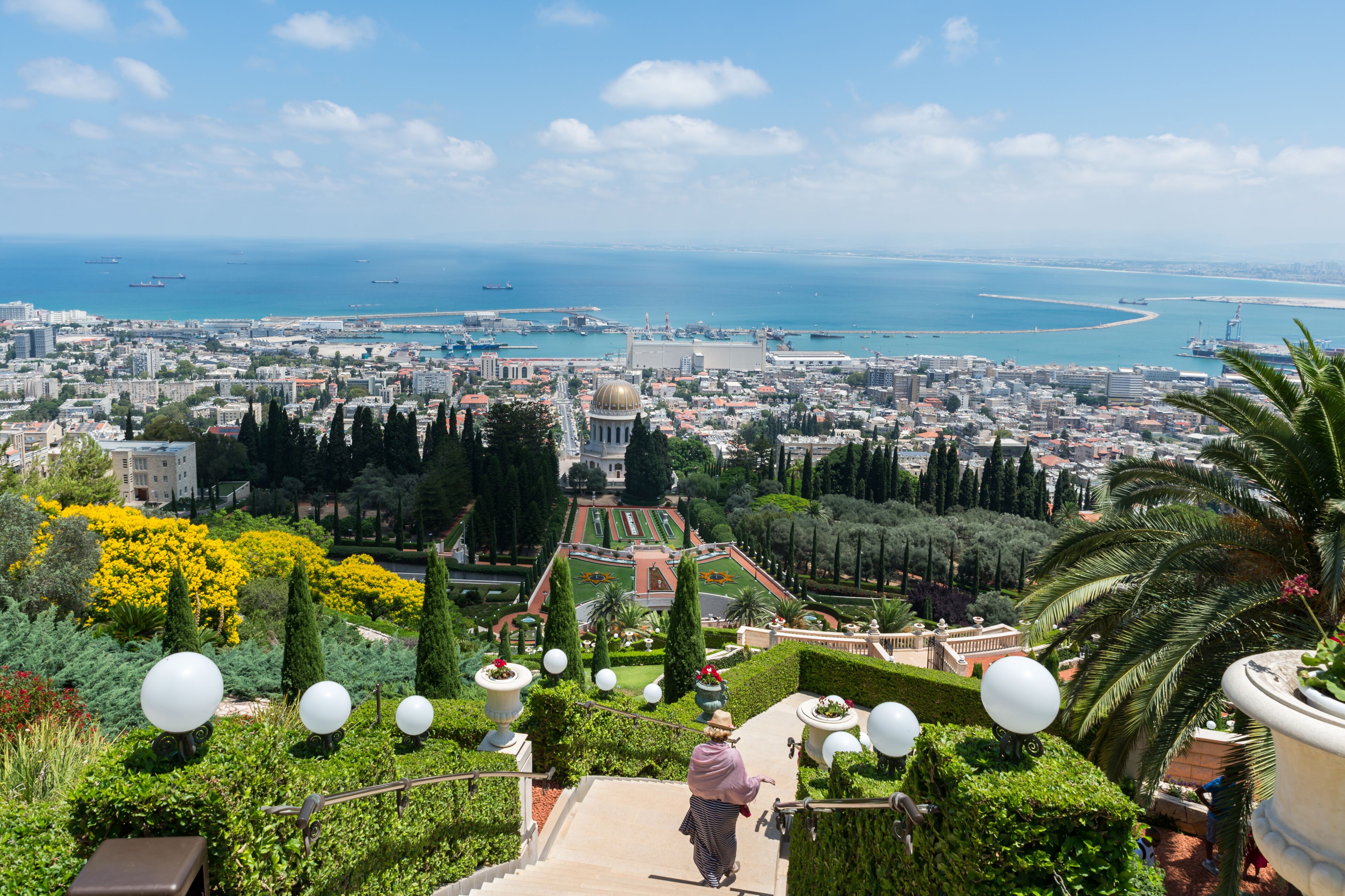 Paisagem urbana com vista para o mar, uma cúpula imponente e um jardim bem cuidado com decorações esféricas.