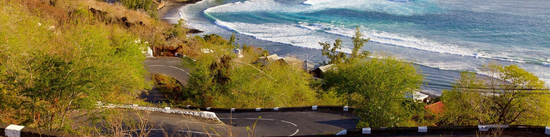 Uma estrada costeira sinuosa seguindo em direção ao oceano, com ondas quebrando na praia.