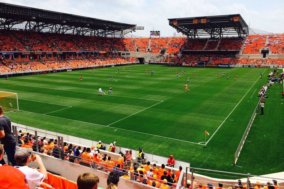 Um estádio de futebol com assentos laranja e um gramado verde.