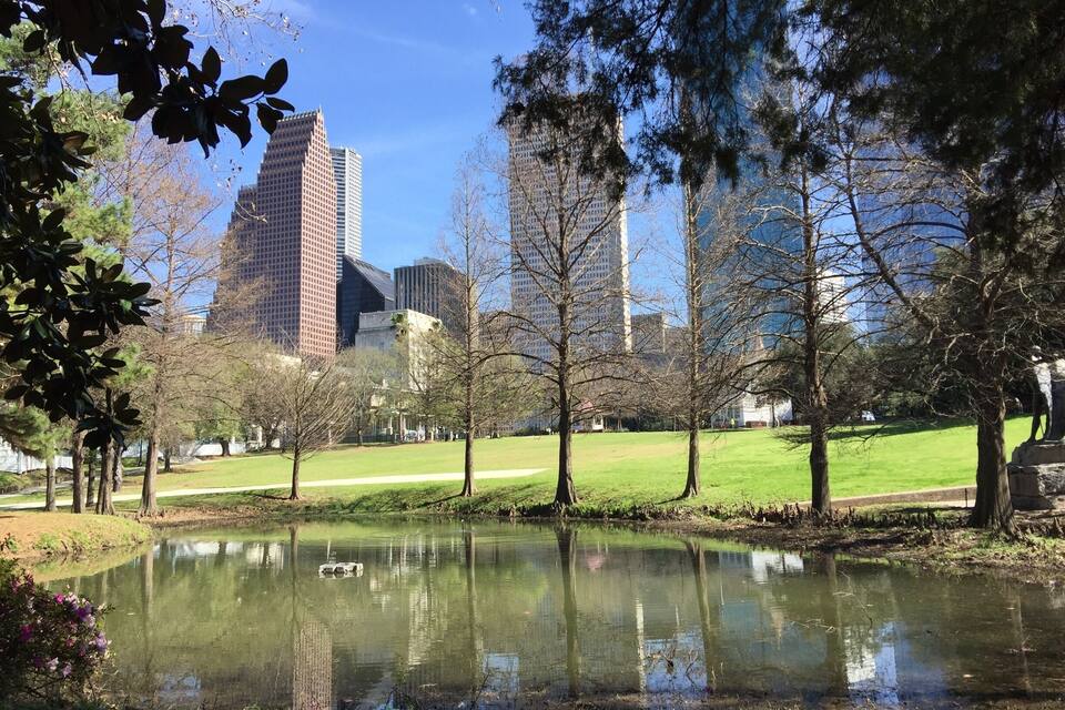 Um parque com lago, árvores e um horizonte urbano ao fundo.