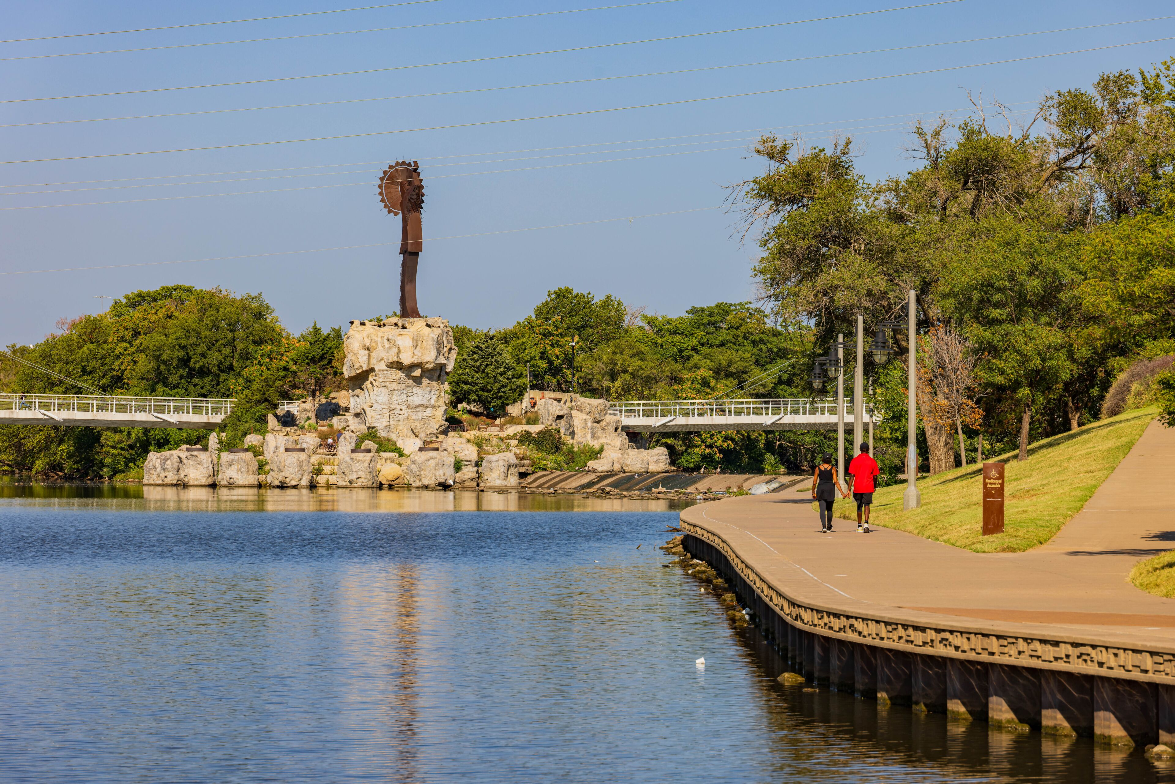 Um parque com uma grande escultura de pedra, uma ponte e um lago calmo.