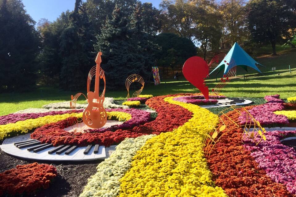Um jardim com canteiros de flores coloridas, uma escultura em formato de guitarra e obras de arte abstratas.