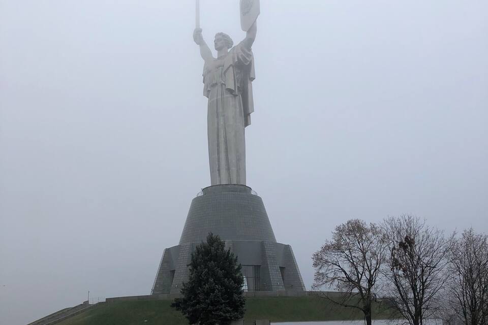 Grande estátua de uma mulher segurando uma tocha e um escudo, erguida sobre um pedestal.