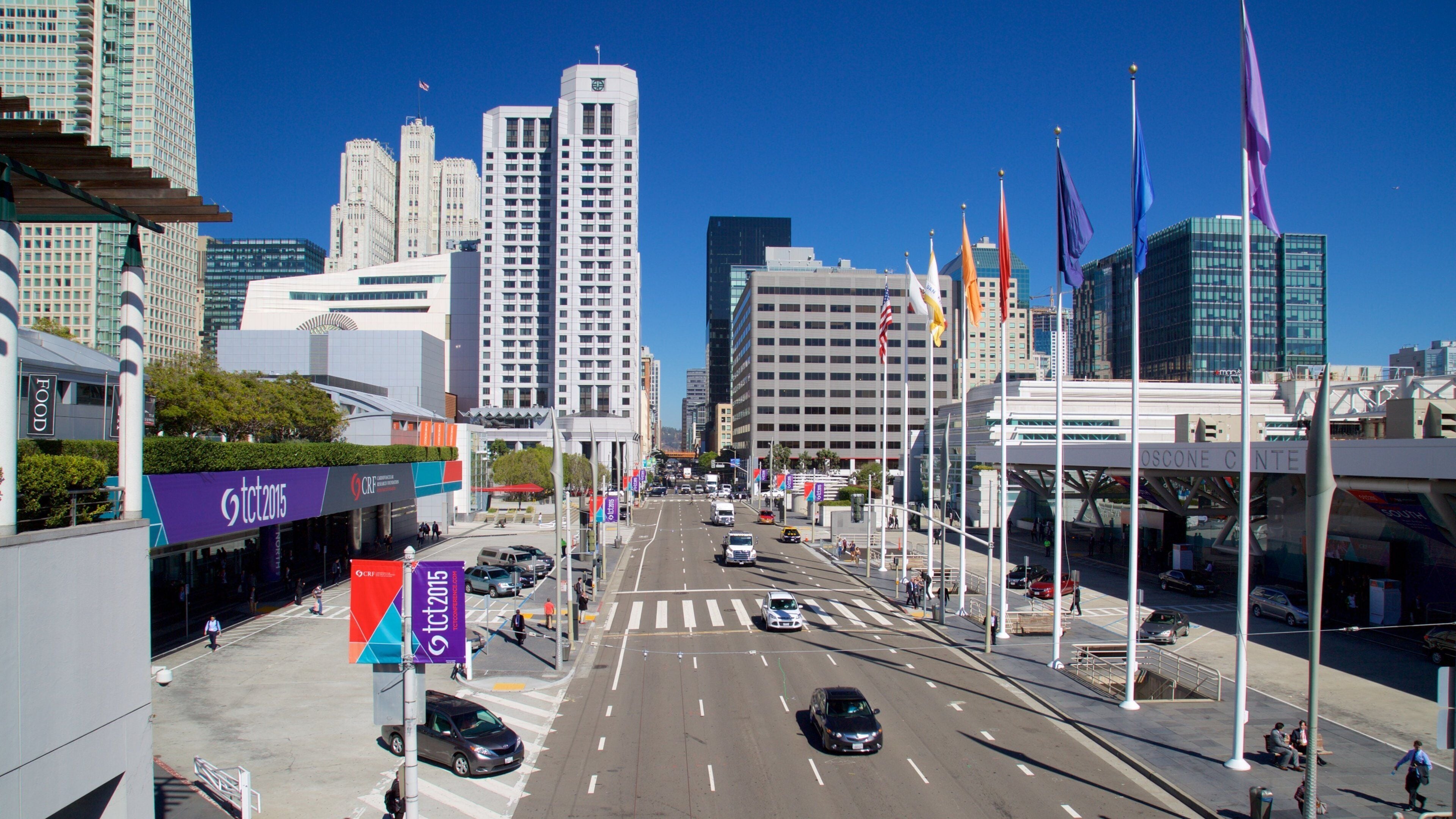 Rua urbana com edifícios altos, bandeiras e carros.